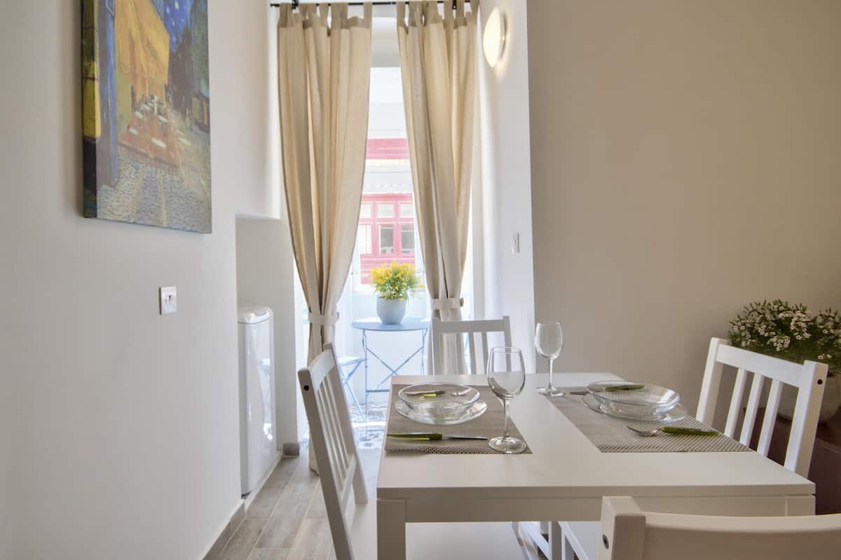 Uma sala de jantar com uma mesa posta para dois, uma planta em vaso e um quadro na parede.