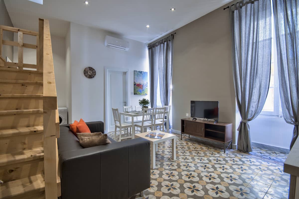 Uma sala de estar moderna com sofá, mesa de centro, rack para TV e área de jantar com cadeiras e mesa.