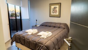 Um quarto moderno com uma cama grande, uma obra de arte emoldurada na parede e vista para a cidade pela janela.