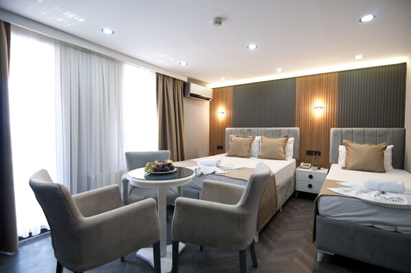 Quarto de hotel moderno com uma cama, duas mesas de cabeceira, uma mesa redonda pequena com cadeiras e uma janela grande com cortinas.
