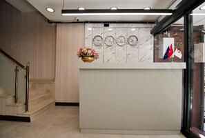Bancada de recepção com parede de mármore, relógios e bandeiras.