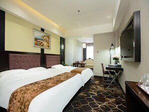 Quarto de hotel com duas camas, uma escrivaninha, uma cadeira, uma televisão e um quadro na parede.