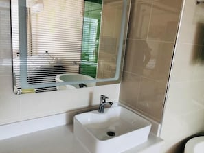 Casa de banho com lavatório branco, espelho e janela com persianas.