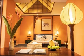 Quarto de hotel com cama, mesa de cabeceira com um vaso de flores, luminária e uma fruteira.