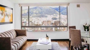 Sala de estar moderna com uma grande janela que oferece vista para a cidade, um sofá, uma mesa de centro e uma poltrona.