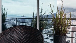 Varanda com móveis de vime, um vaso de planta e vista para a cidade.