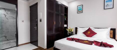 Quarto de hotel com uma cama grande, guarda-roupa de madeira escura, uma porta de vidro e uma pequena planta em vaso.