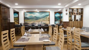 Um restaurante com mesas e cadeiras de madeira, quadros nas paredes e diversos equipamentos de cozinha.