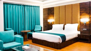 Quarto de hotel com uma cama grande, duas poltronas, uma mesinha e chão de madeira.