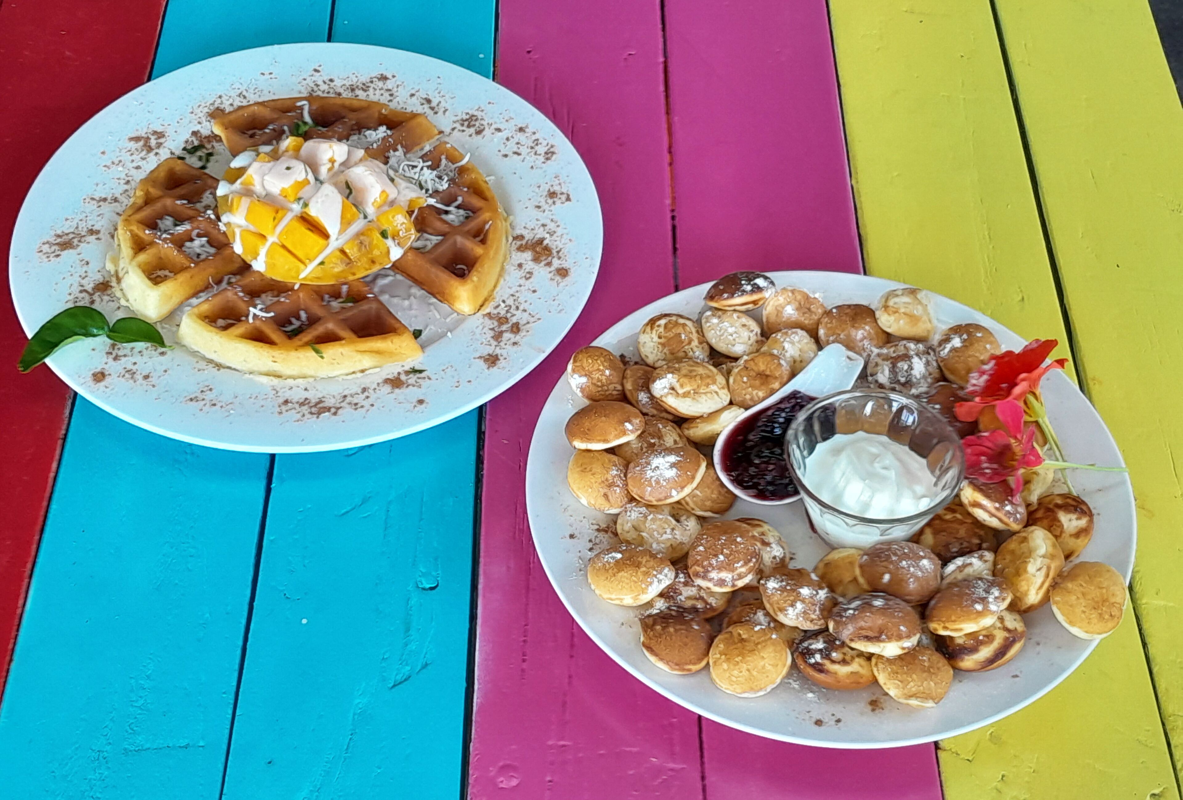 Duas travessas de comida sobre uma mesa de madeira colorida.