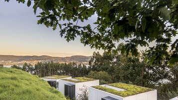 Uma fileira de edifícios modernos, brancos e em forma de caixa, com telhados planos cobertos de grama, com um horizonte de paisagem montanhosa e uma cidade ao longe.