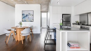Uma cozinha moderna com armários brancos, uma geladeira de aço inoxidável e uma ilha planejada com banquetas.