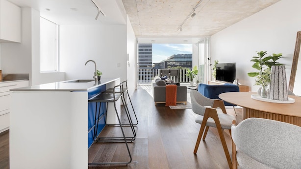 Cozinha moderna com uma ilha grande, sala de jantar com mesa e cadeiras de madeira, e sala de estar com sofá e televisão.