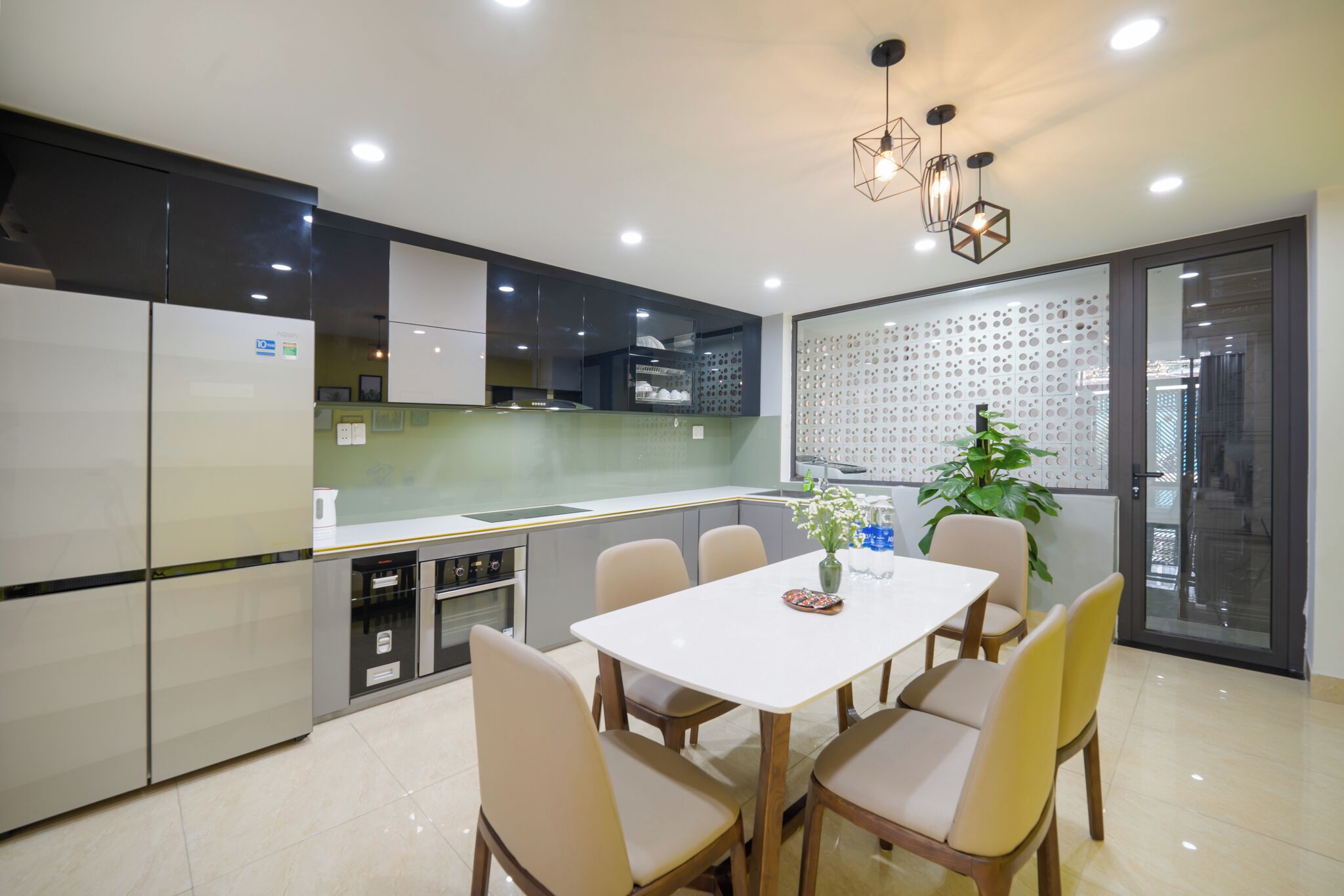 Cozinha moderna com área de refeições, destacando uma mesa e cadeiras brancas, um vaso de planta e um painel decorativo na parede.