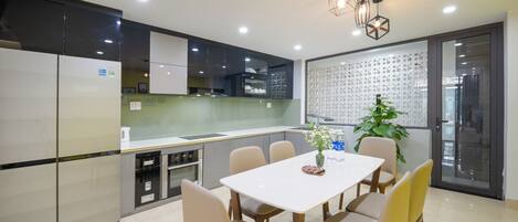 Cozinha moderna com área de refeições, destacando uma mesa e cadeiras brancas, um vaso de planta e um painel decorativo na parede.