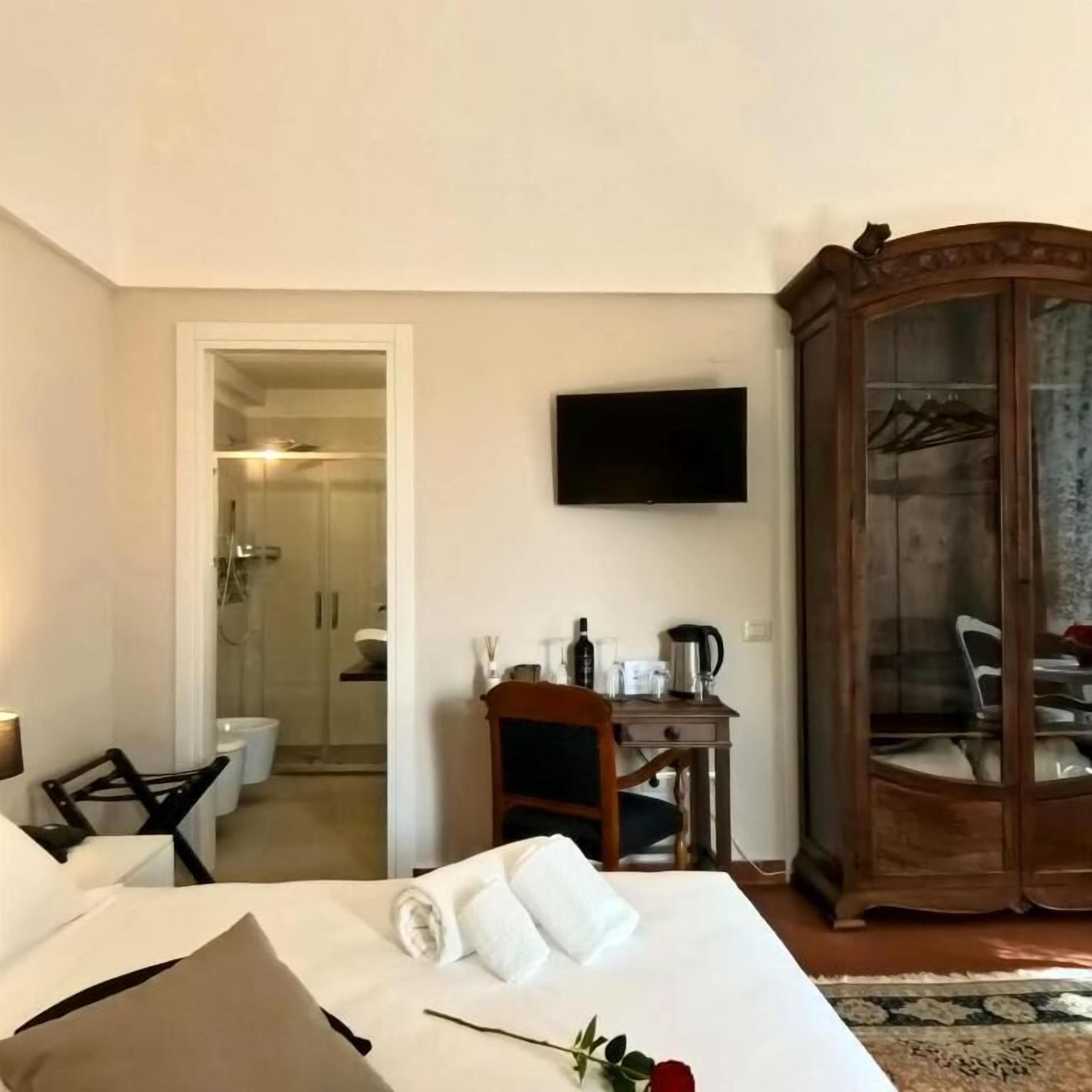 Quarto de hotel com uma cama, um armário de madeira com espelho, uma televisão na parede e uma pequena mesa com uma cadeira.
