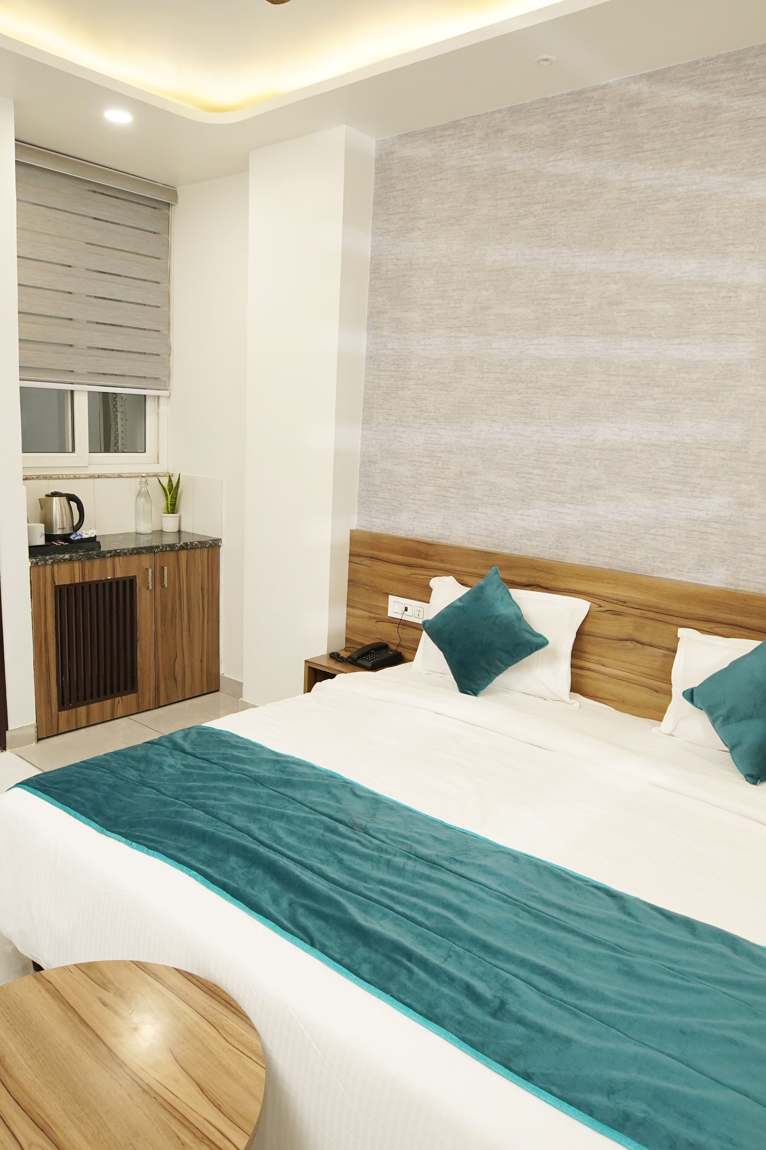 Quarto de hotel moderno com uma cama grande, cabeceira de madeira e uma pequena cozinha equipada.