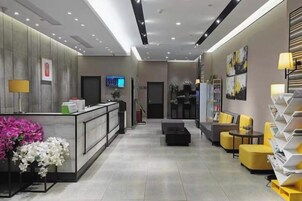 Um saguão de hotel com balcão de recepção, área de estar e escadas que levam a outros andares.