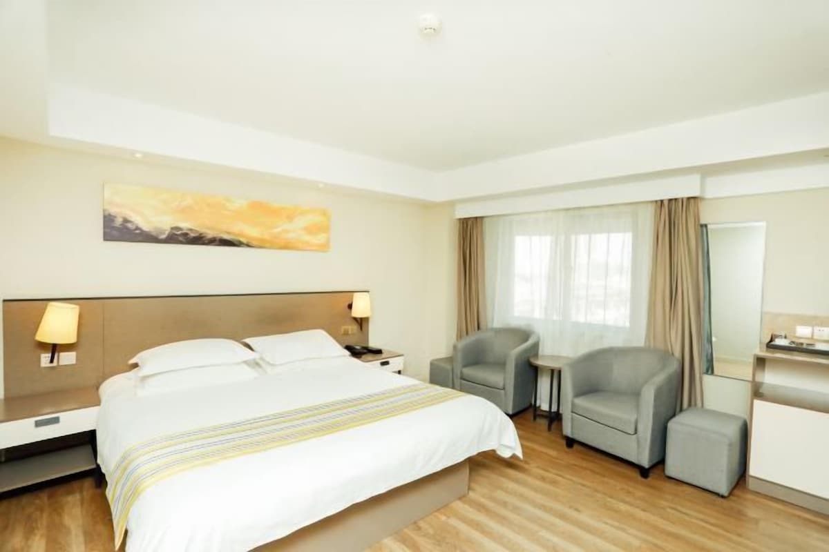 Quarto de hotel com uma cama, duas poltronas, uma mesinha, uma escrivaninha e um espelho.