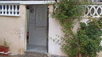 Um edifício residencial com fachada branca, porta e um pequeno jardim com plantas em vasos.