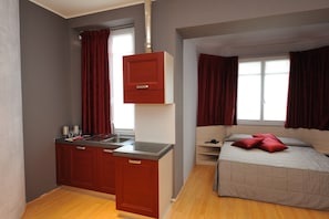Quarto compacto com cozinha compacta, cama e janela com cortinas.