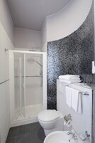 Um banheiro moderno com chuveiro em cabine de vidro, vaso sanitário branco e pia com espelho.