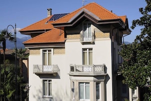 Um edifício de dois andares com telhado de telhas vermelhas, varandas com grades de metal e fachada decorativa.