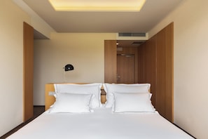 Quarto de hotel moderno com cama bem arrumada, luminária de cabeceira e guarda-roupa de madeira.