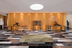 Um lobby com parede de madeira, um lustre oval grande e duas mesas com esculturas.