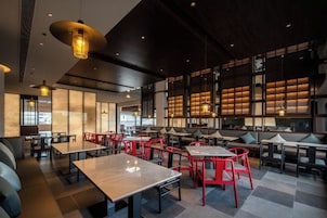 Interior moderno de restaurante com pé-direito alto, paredes de tijolo aparente e diferentes opções de assentos, incluindo mesas e cabines.
