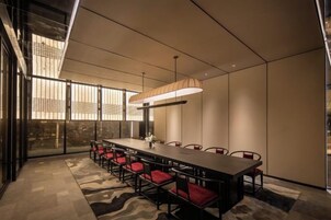 Sala de conferências com uma mesa comprida, cadeiras vermelhas e uma luminária pendente moderna.