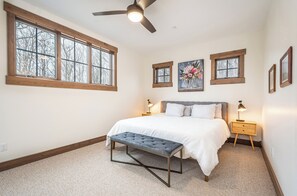 Quarto com uma cama grande, duas mesas de cabeceira, um banquinho e várias janelas.