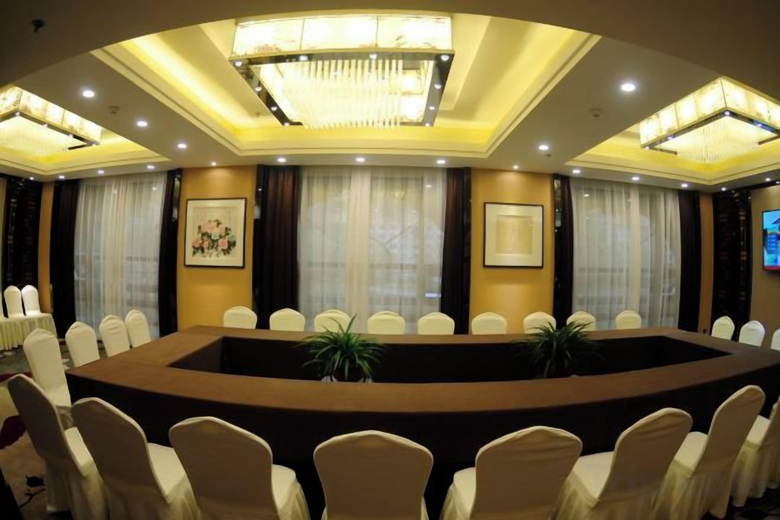 Uma sala de conferências com uma mesa redonda, cadeiras brancas e um lustre.