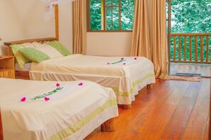 Quarto com duas camas, piso de madeira, varanda com guarda-corpo e janela com cortinas.