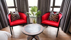 Quarto com duas cadeiras vermelhas estofadas com almofadas de padrão de zebra, uma mesa redonda pequena com design geométrico e uma planta em vaso no centro.
