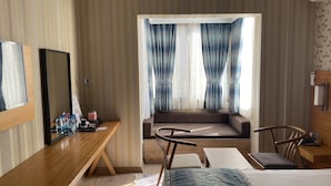 Quarto de hotel com cama, escrivaninha, poltrona, sofá e janela com cortinas.