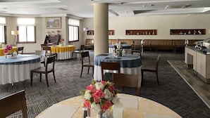 Uma área de refeições de hotel com mesas redondas, cadeiras e um buffet.
