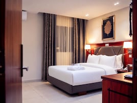 Quarto de hotel com cama, abajures, mesa de cabeceira de madeira e uma obra de arte emoldurada na parede.