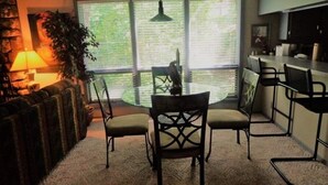 Uma sala de jantar com uma mesa redonda, quatro cadeiras, um vaso com planta e vista para o verde lá fora.