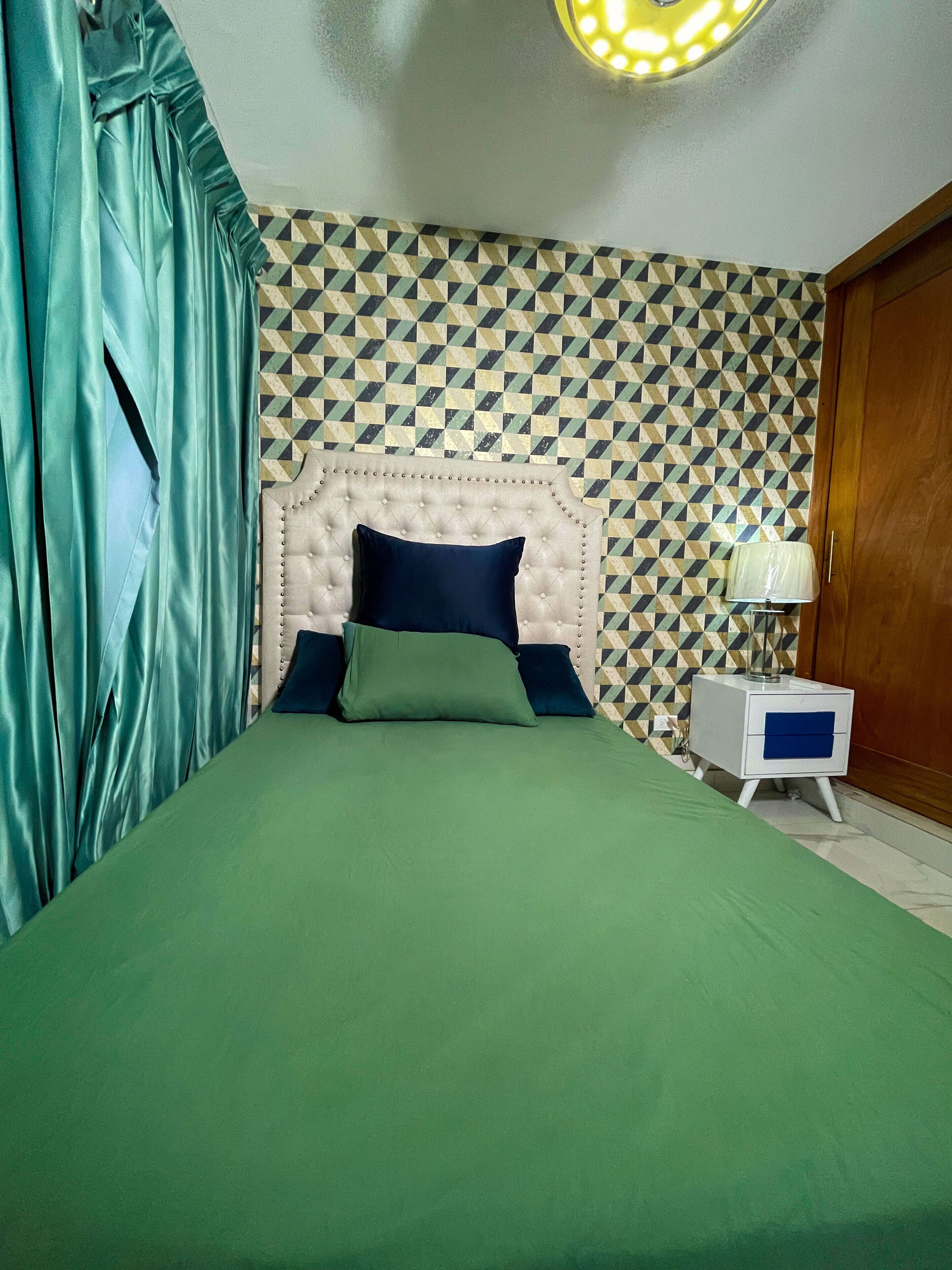 Quarto com cama, mesa de cabeceira, abajur e parede estampada.