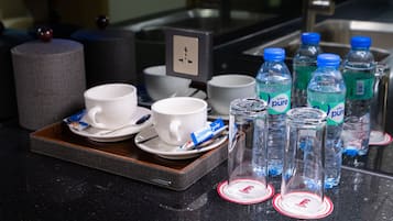 Disposição de café da manhã em quarto de hotel, com xícaras, pires brancos e uma bandeja, além de várias garrafas de água e um copo.