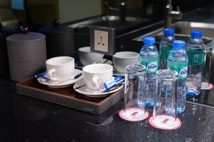 Disposição de café da manhã em quarto de hotel, com xícaras, pires brancos e uma bandeja, além de várias garrafas de água e um copo.