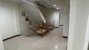 Um corredor amplo com piso de azulejos, escada de madeira e corrimão de metal.