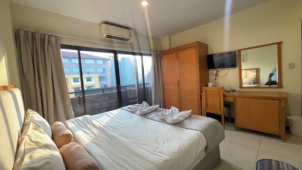 Quarto de hotel com uma cama grande, escrivaninha, guarda-roupa, televisão e janela com cortinas.