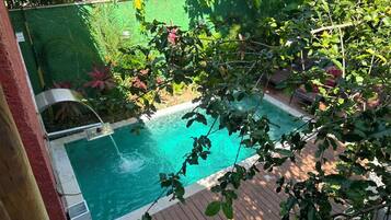 Uma piscina com deck de madeira, rodeada por vegetação exuberante e uma cerca verde.