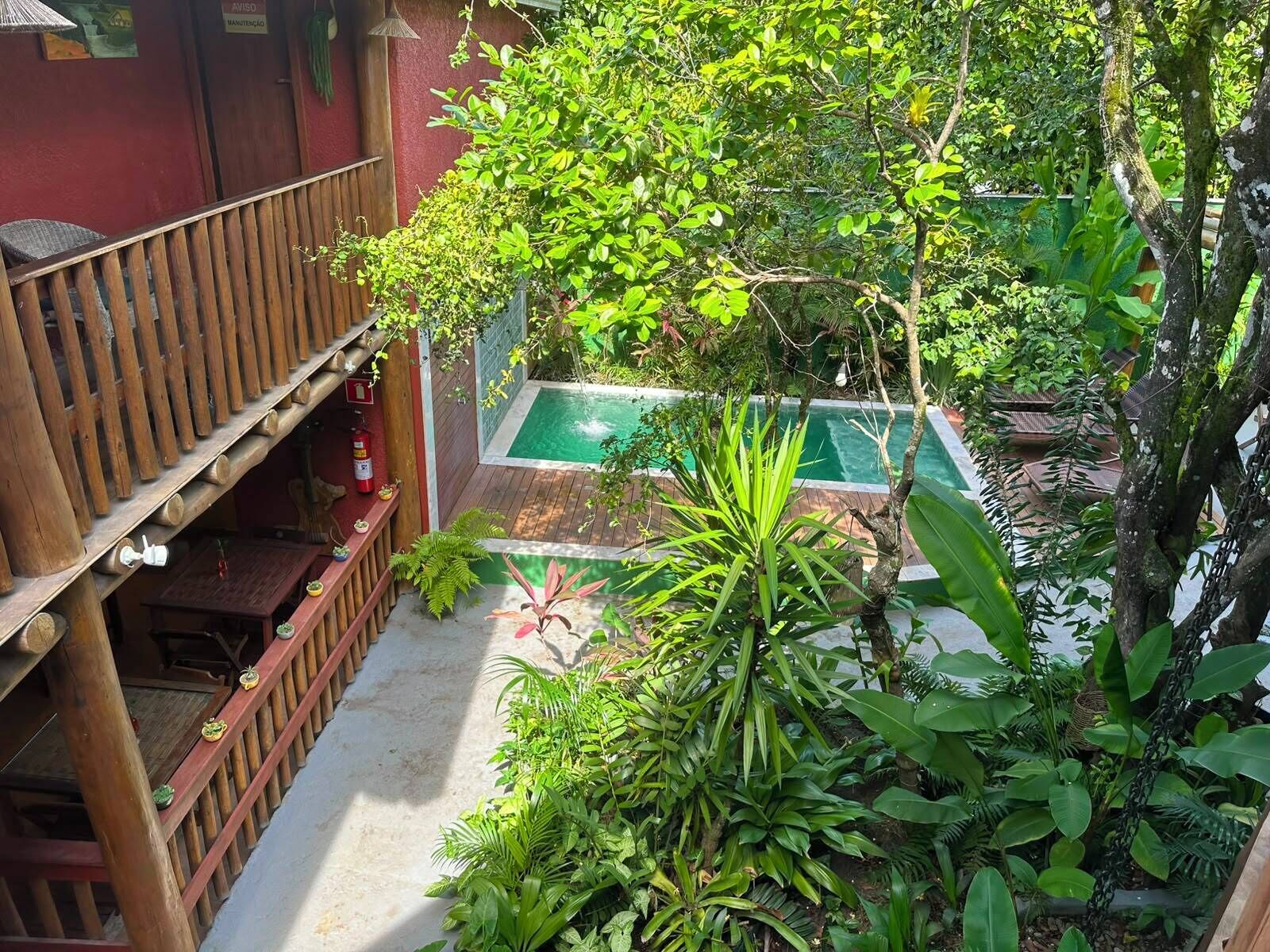 Uma piscina rodeada por vegetação exuberante, um deck de madeira e um edifício vermelho.