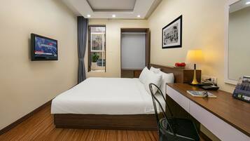 Quarto de hotel com cama, escrivaninha com luminária, televisão na parede e janela com cortinas.