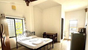 Quarto com cama, escrivaninha, cadeira, ventoinha no teto e geladeira.