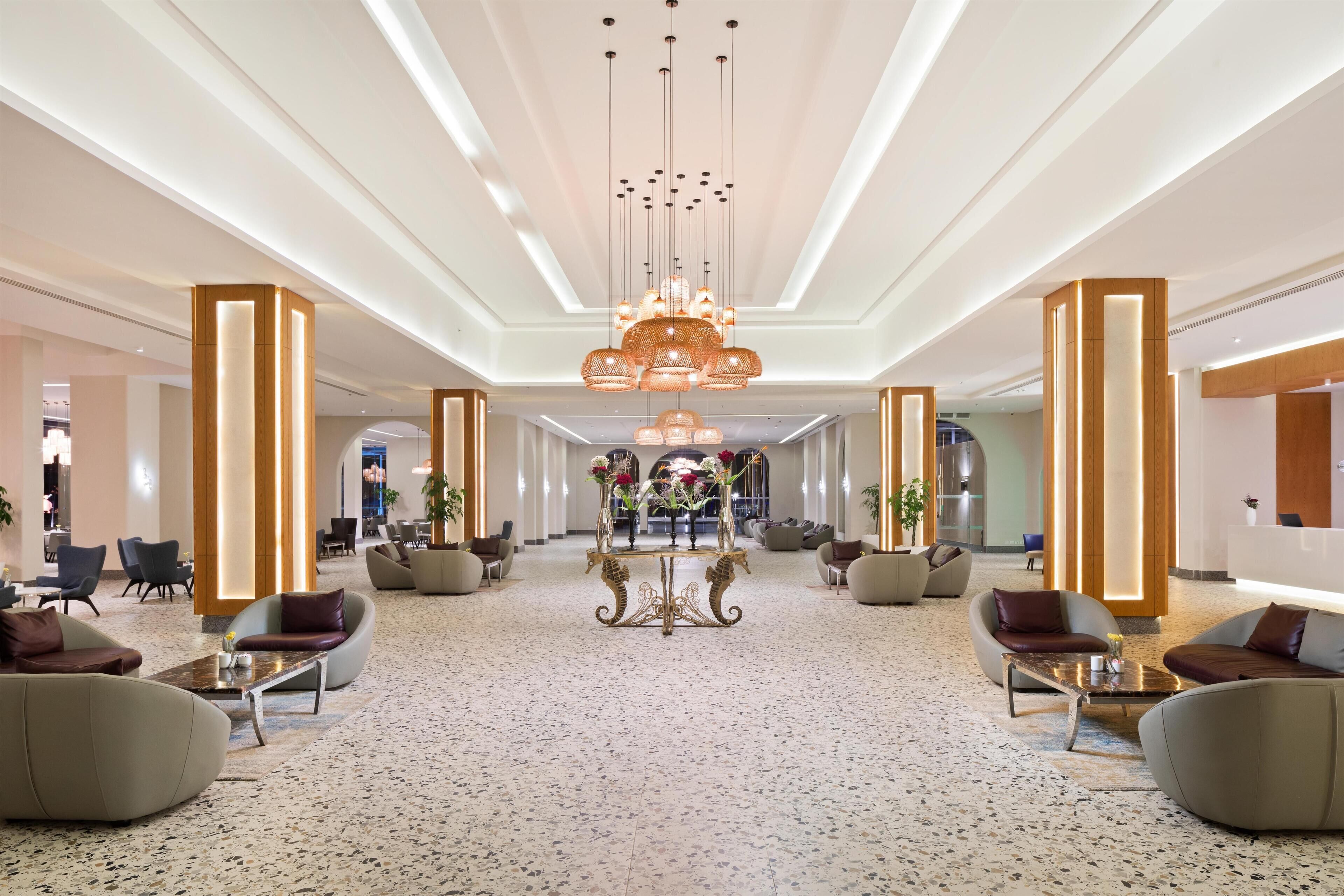 Um hall amplo com uma mesa central ricamente decorada, assentos modernos e um candelabro.