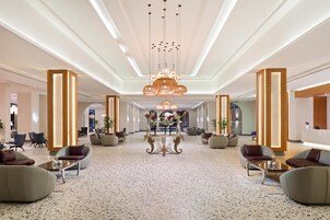 Um hall amplo com uma mesa central ricamente decorada, assentos modernos e um candelabro.